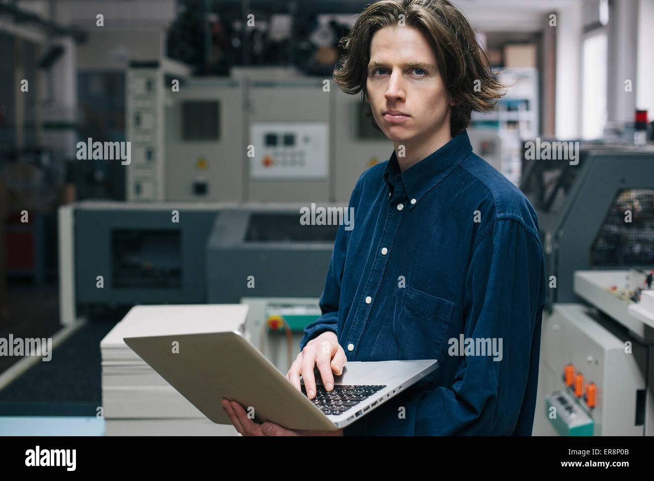 Portrait of confident young male technician using laptop in factory ...