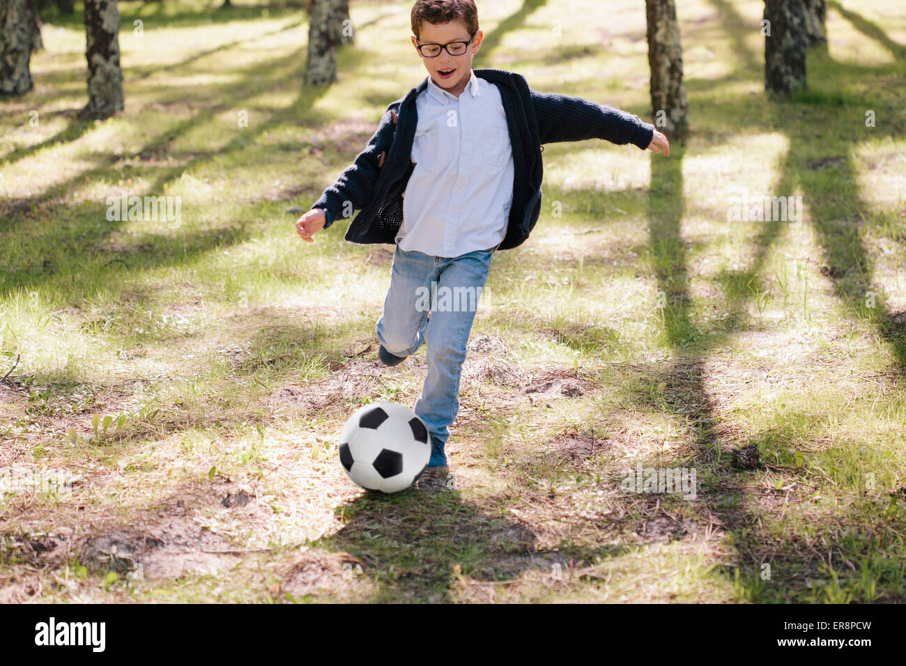Full length of happy boy playing soccer in forest Stock Photo - Alamy