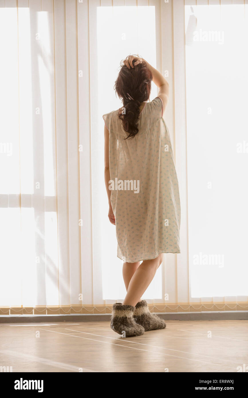 Rear view of woman looking through window at home Stock Photo - Alamy