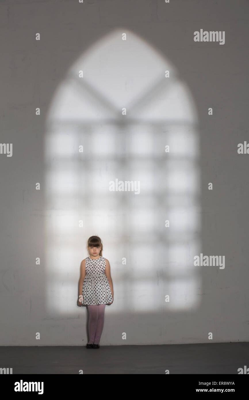 Shadow of window falling on girl standing against white wall at home ...