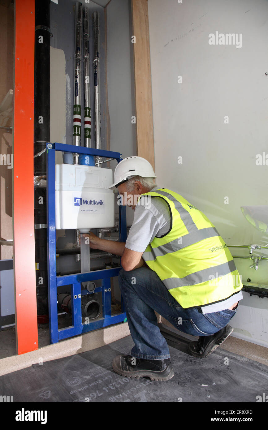 A plumber installs piping and cistern frames to the toilets in a new ...