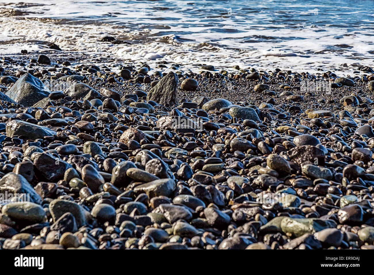 Stones and water with waves on the beach coast or shore of ocean or sea ...