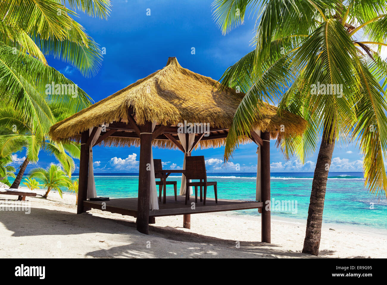 Tropical gazebo and two chairs on an sandy island beach with coconut ...