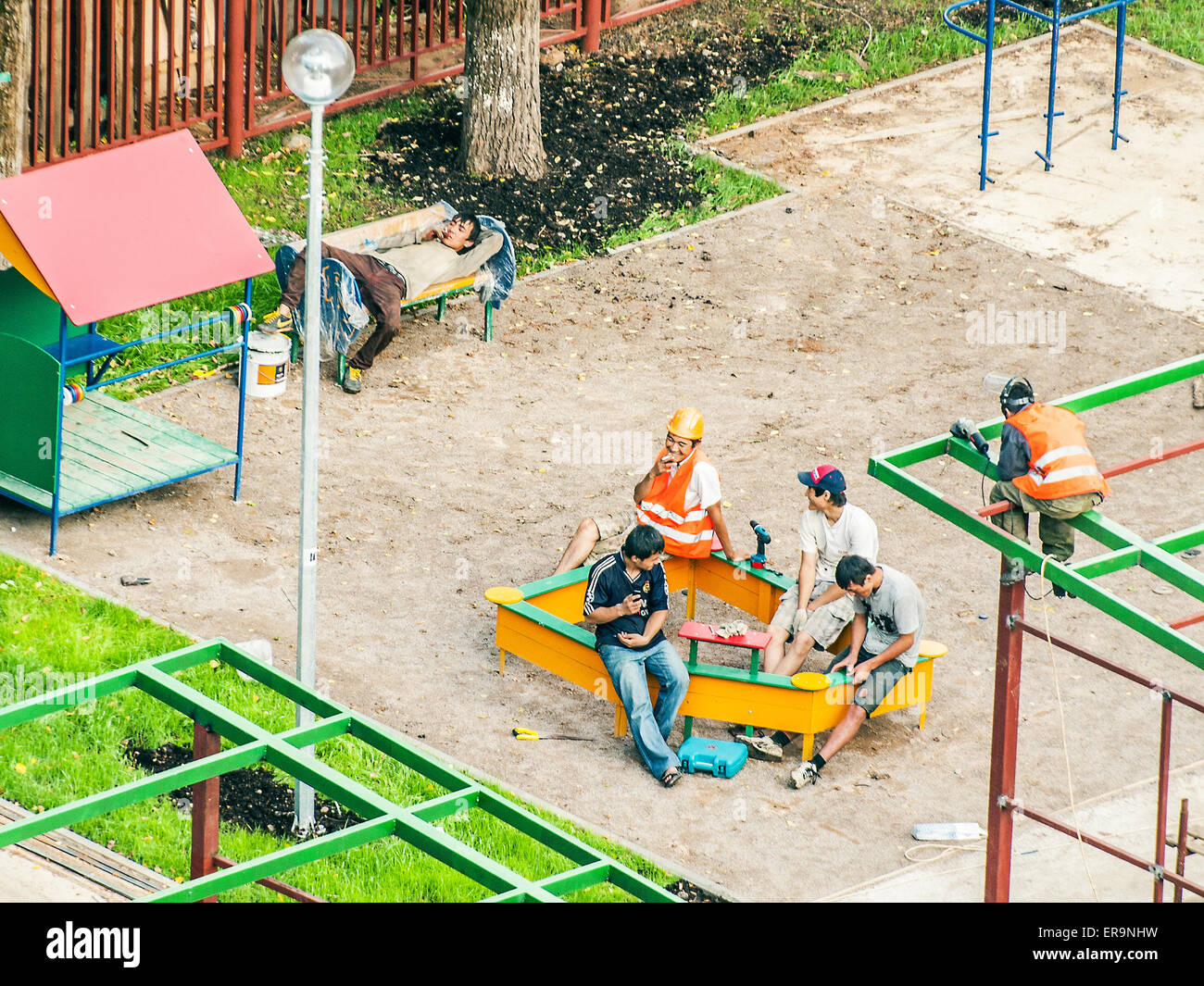 Asian builders smoke and relax on the under-construction playground ...