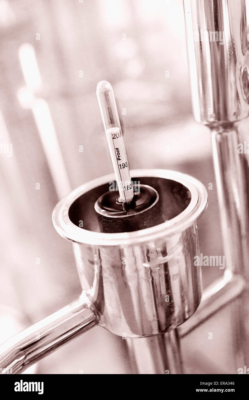 Alcoholmeter floating in alcohol at craft distillery. Vertical sepia ...