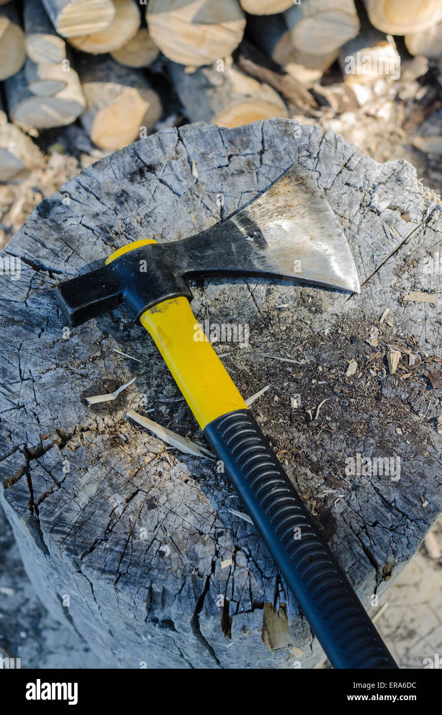 Yellow axe with a piece of wood near a stack of logs Stock Photo - Alamy