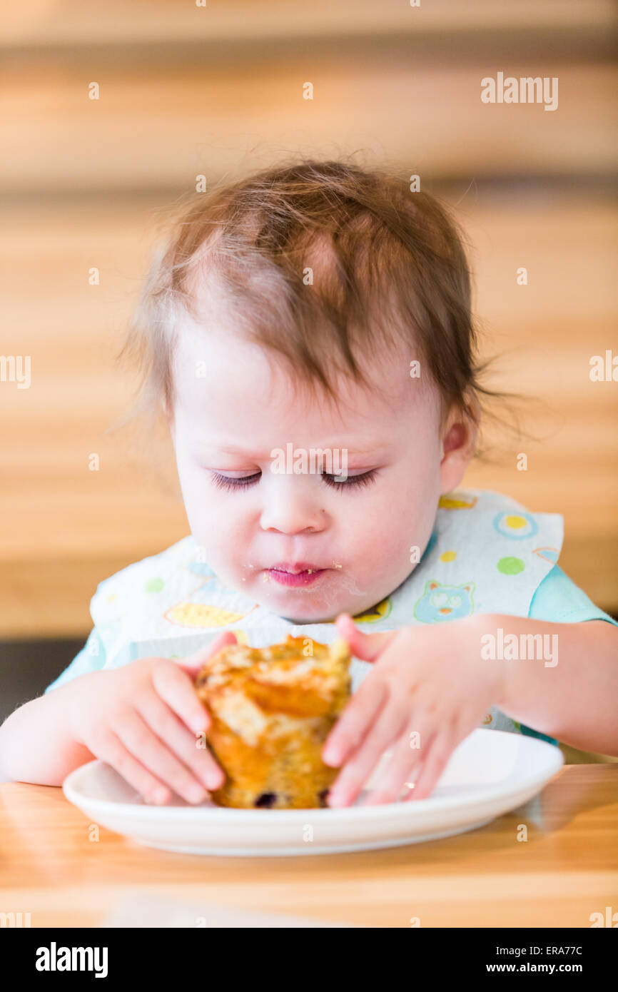 Little cute girl eating muffin at the restaurant Stock Photo - Alamy