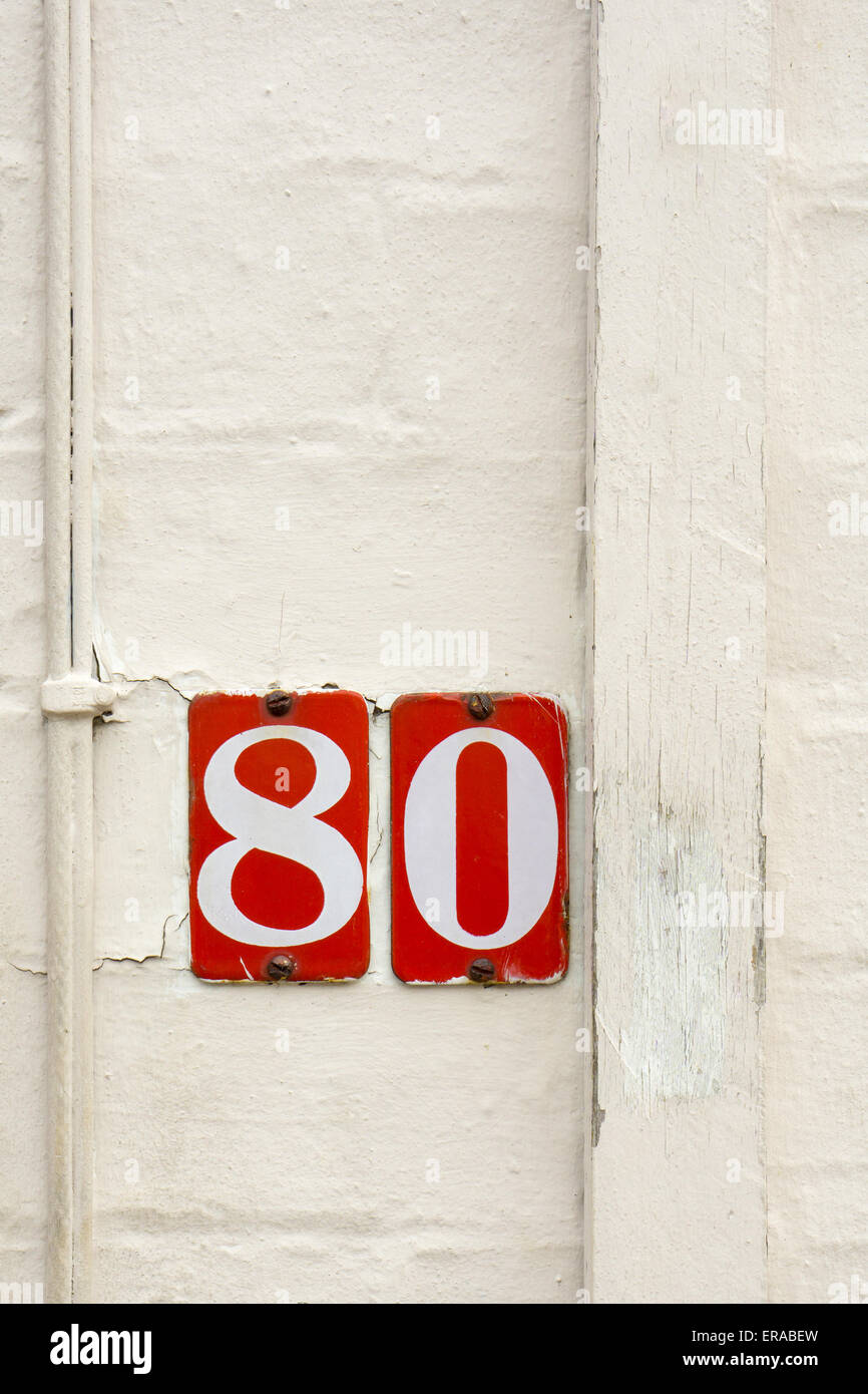 Red plate numbers Number 80 eighty on white painted surface closeup ...