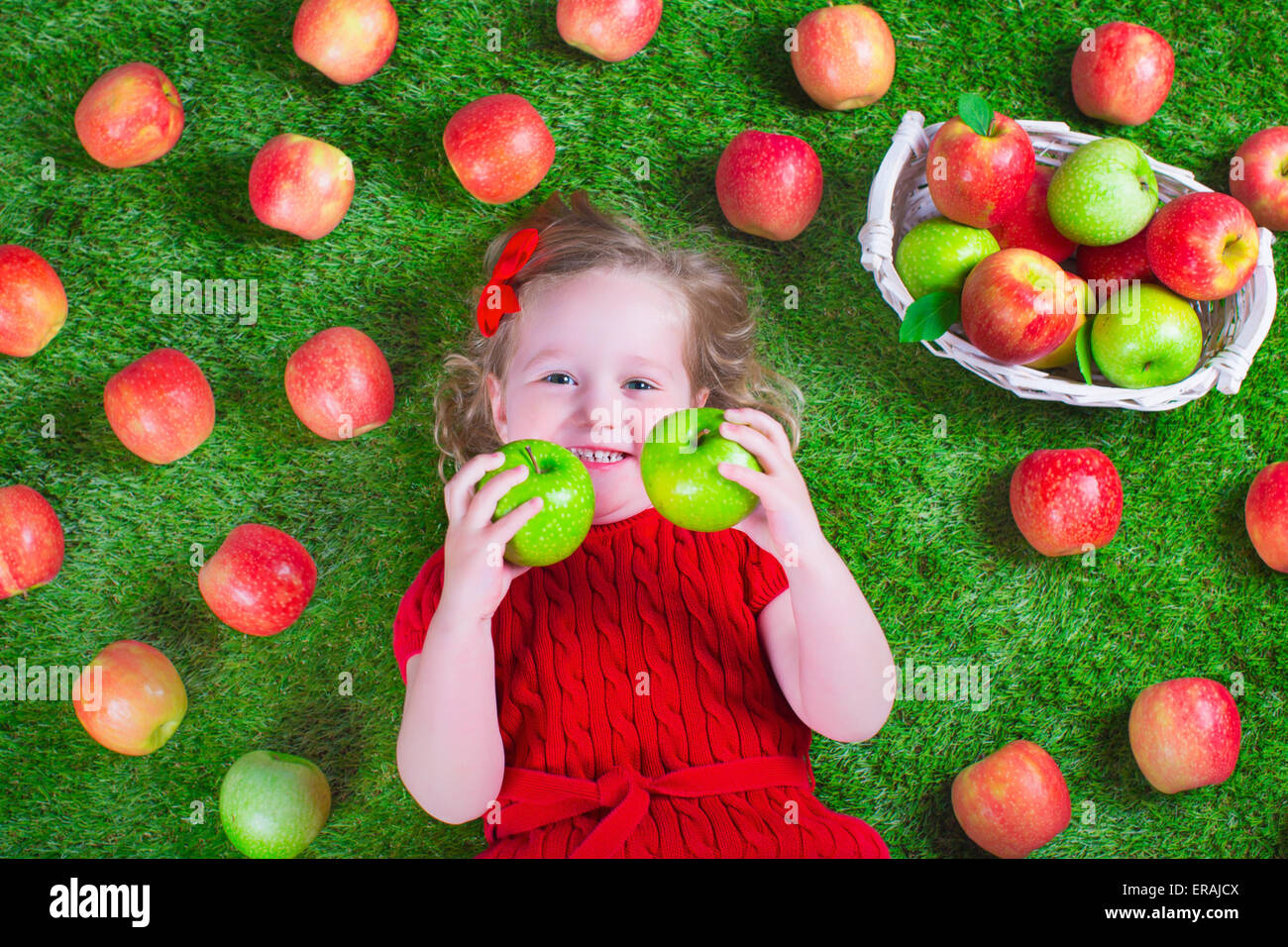 Child eating apple. Little girl playing peek a boo holding fresh ripe ...