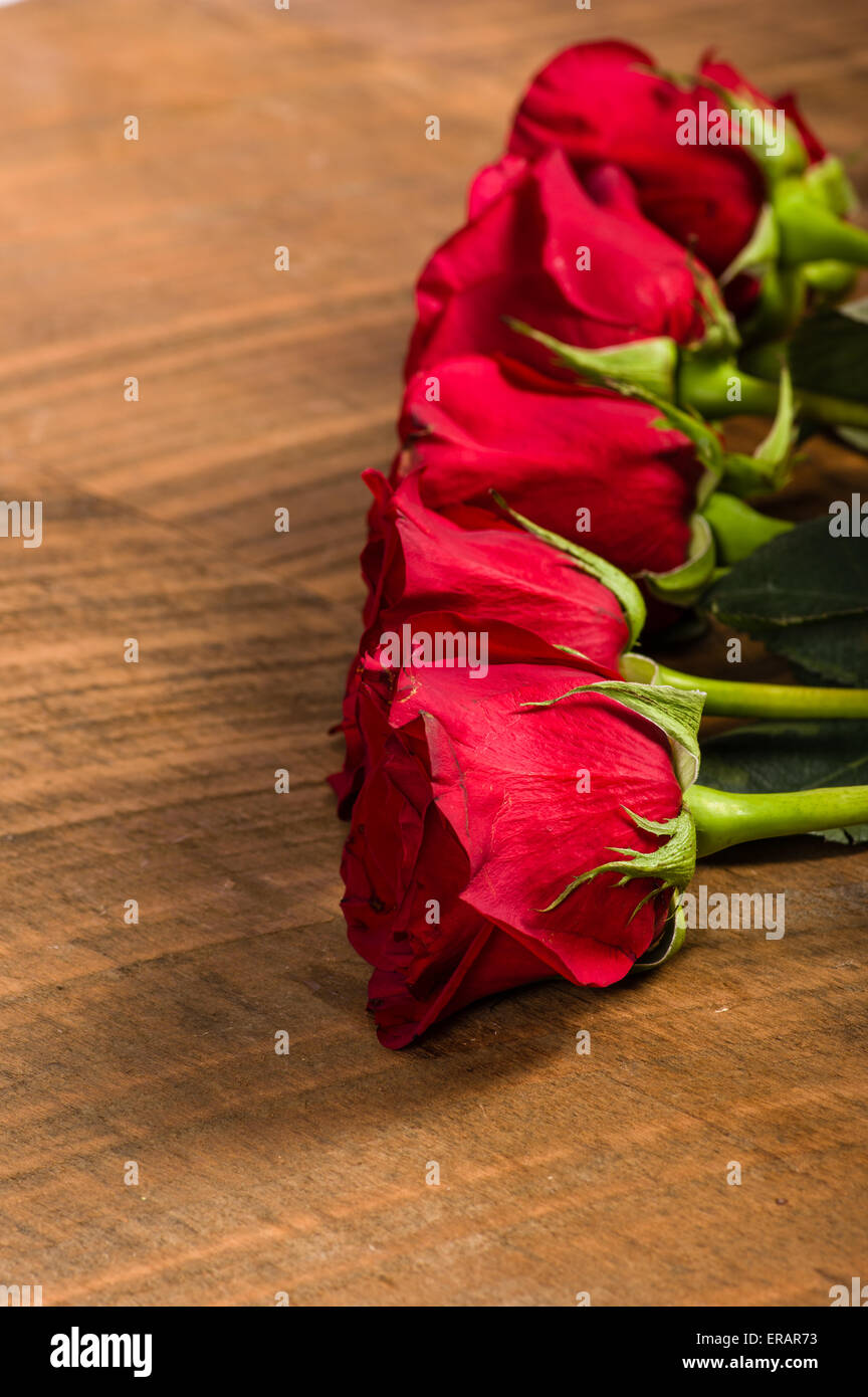 Bright red roses in a row on a wooden table Stock Photo - Alamy