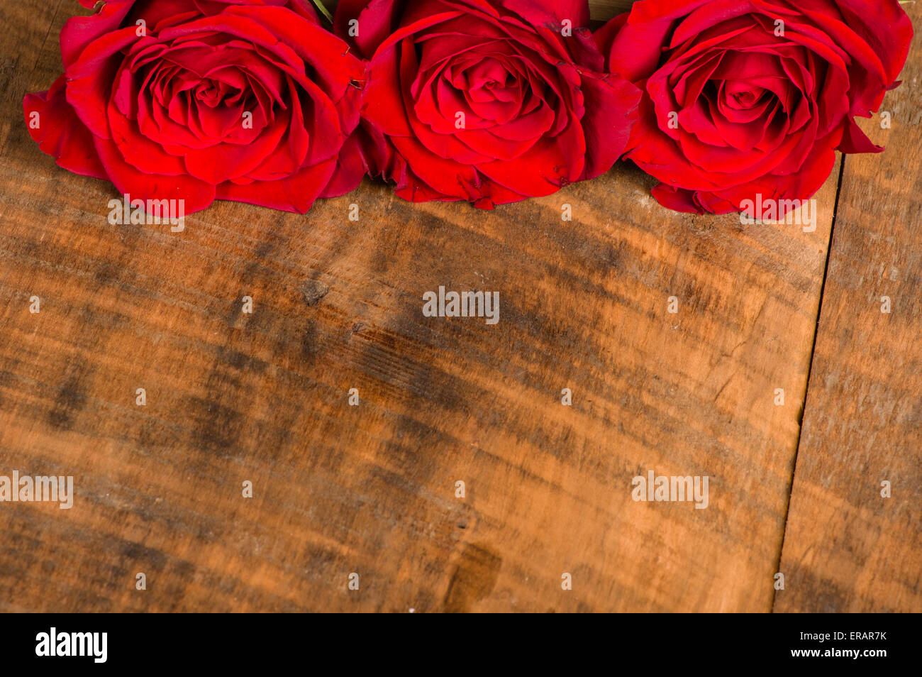 Three bright red roses on a wooden table Stock Photo - Alamy