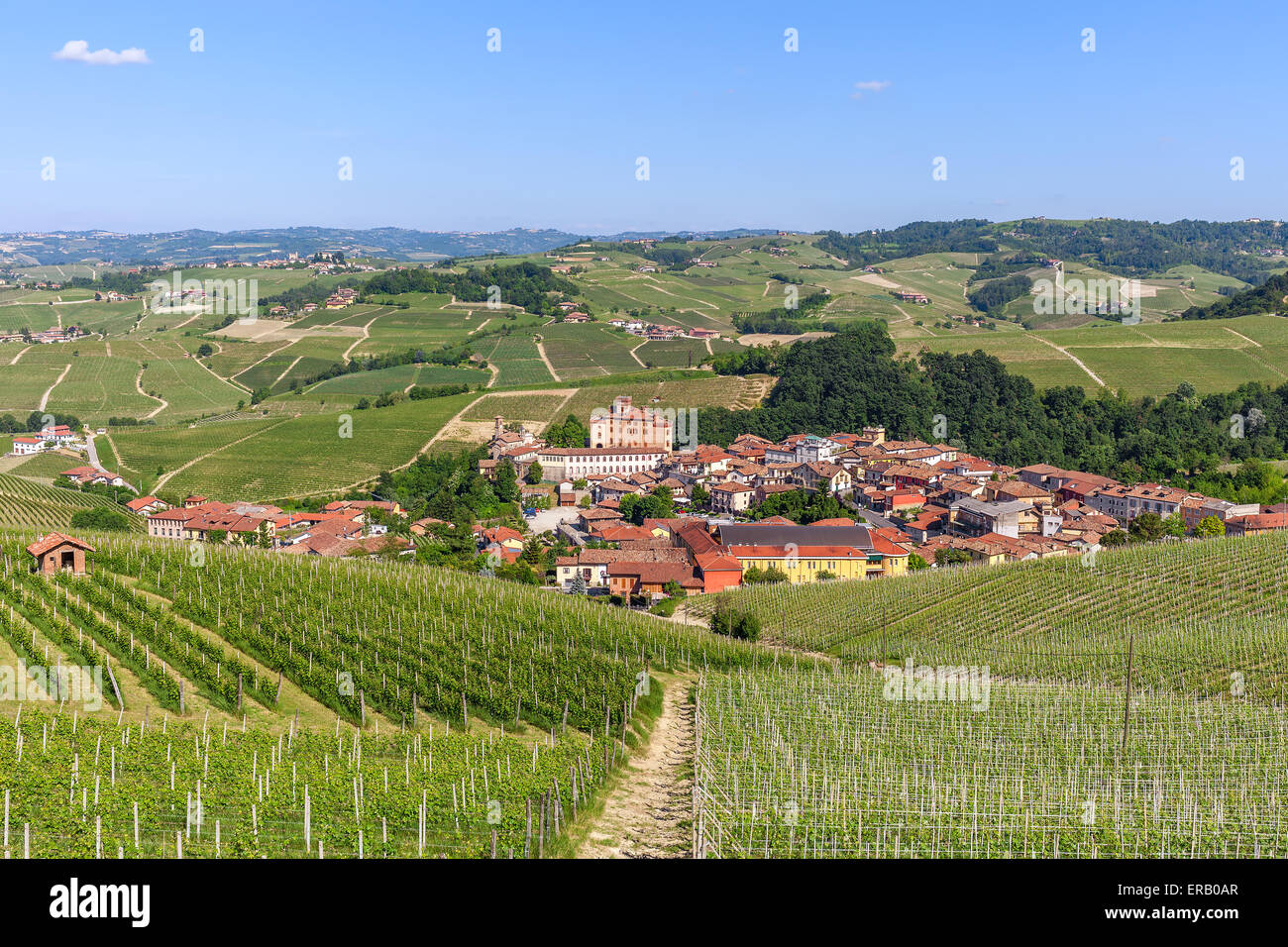Small town of Barolo among hills with green vineyards under blue sky in ...