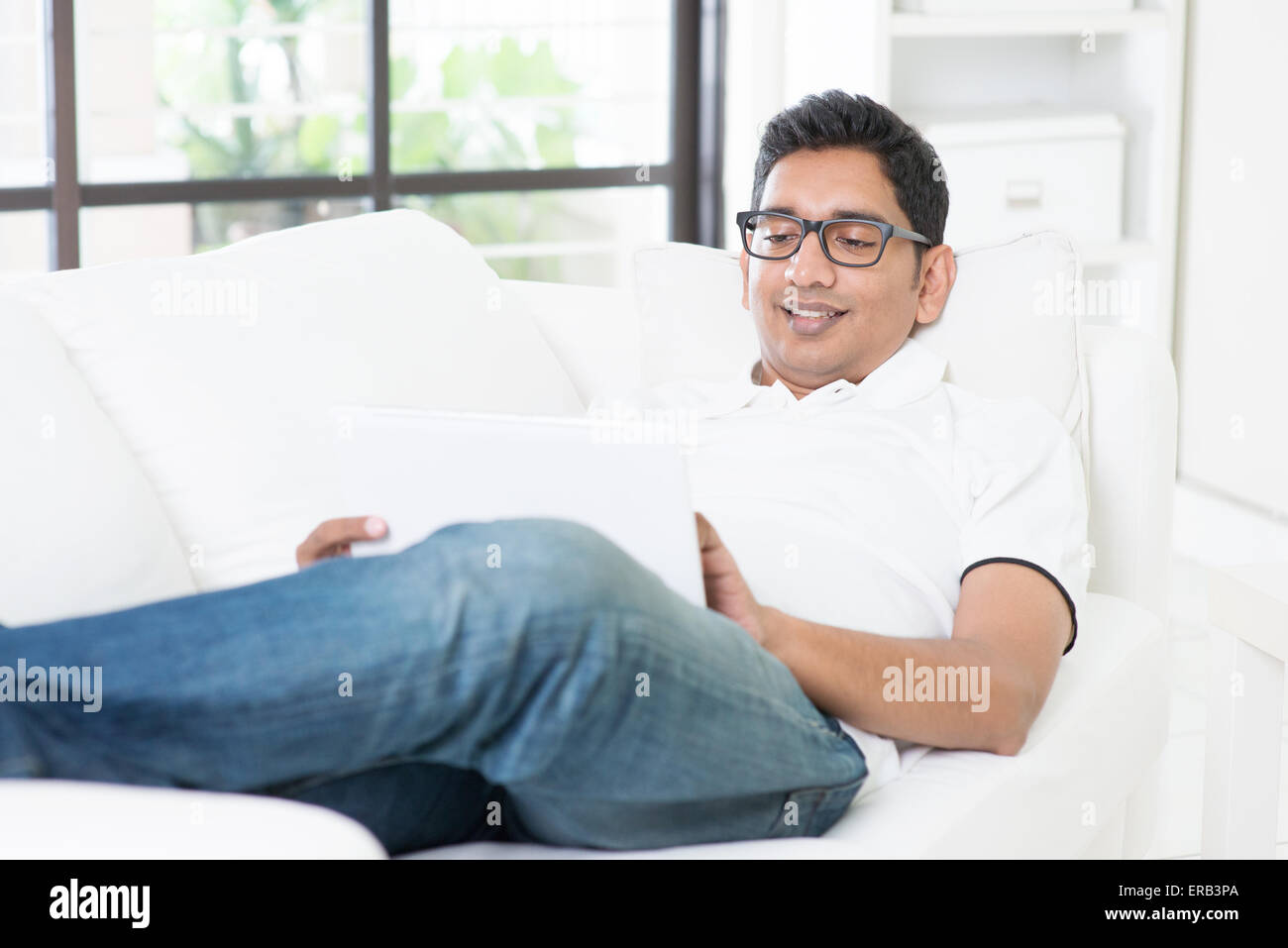 Indian guy using digital computer tablet at home. Asian man relaxed and ...