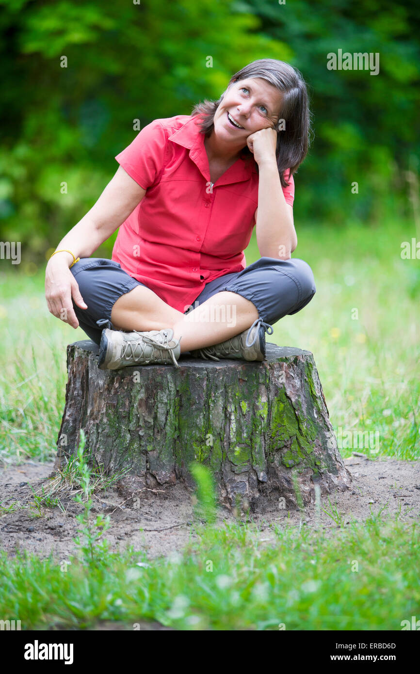 older woman sitting on a tree stump and smiles Stock Photo - Alamy