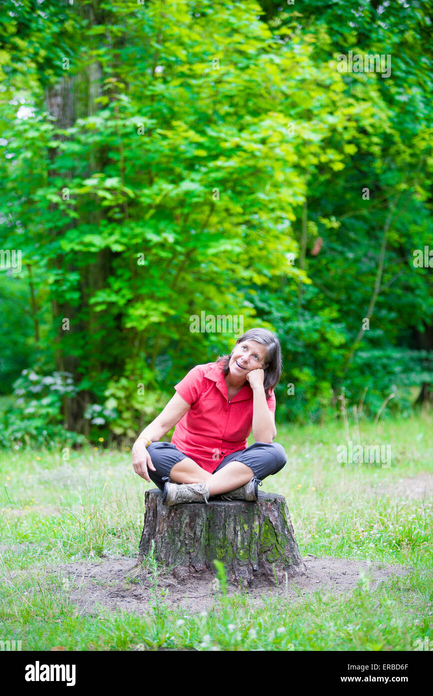 older woman sitting on a tree stump and smiles Stock Photo - Alamy