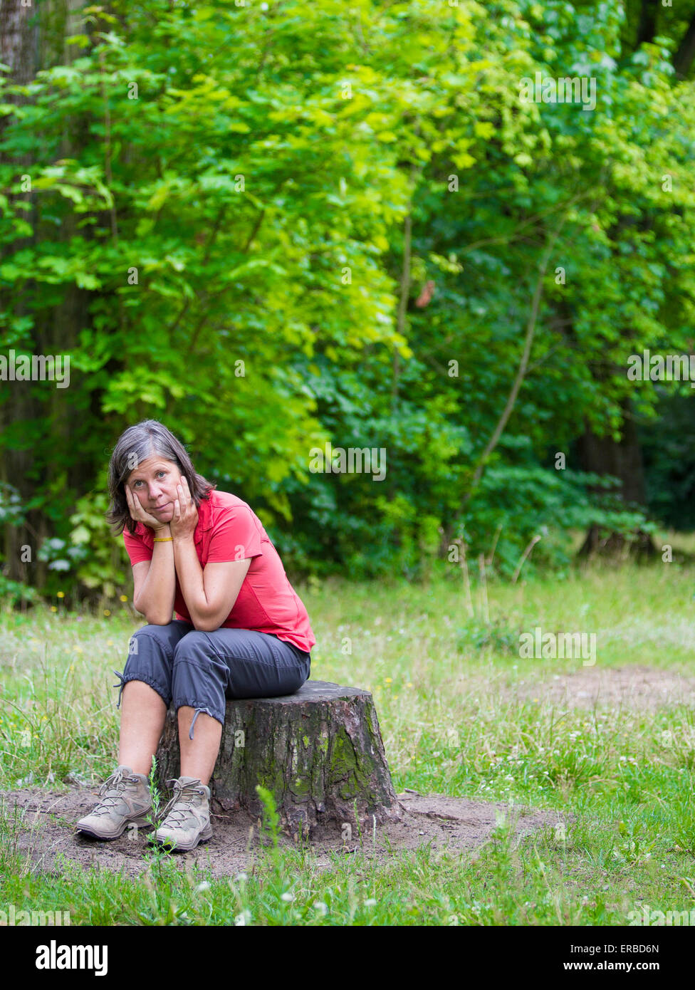 older woman sitting on a tree stump and looking sad Stock Photo - Alamy