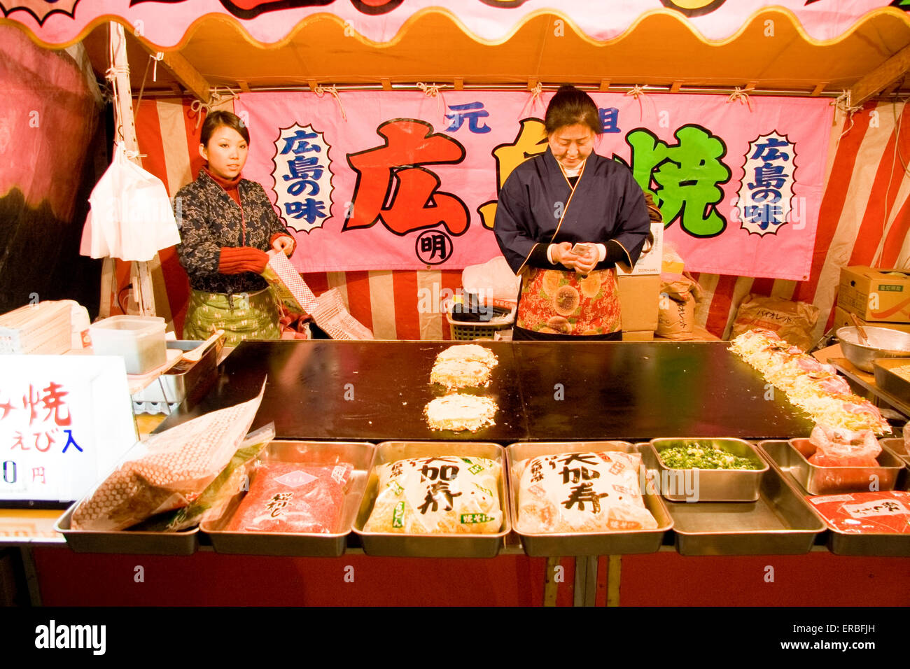 Two Japanese women, facing, preparing Hiroshima yakisoba, fried noodles ...