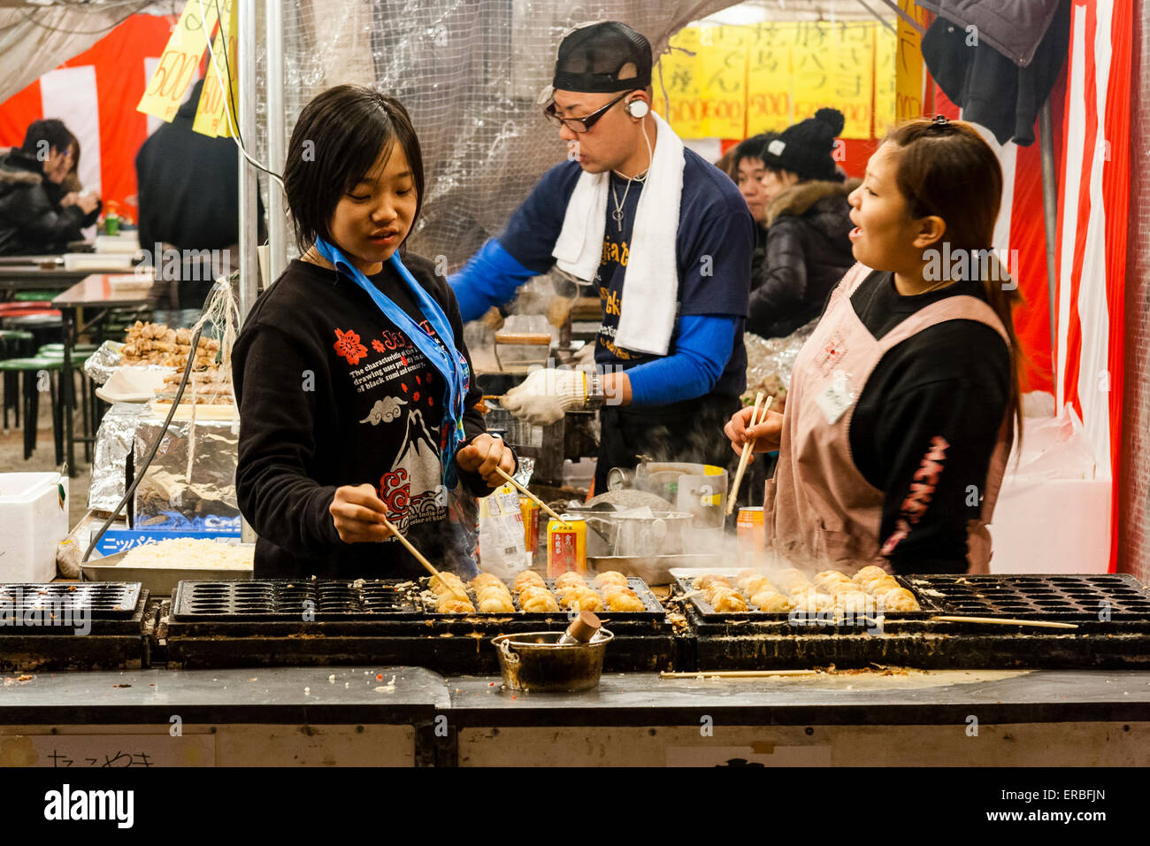 Two Japanese women chatting to each other while cooking takoyaki ...
