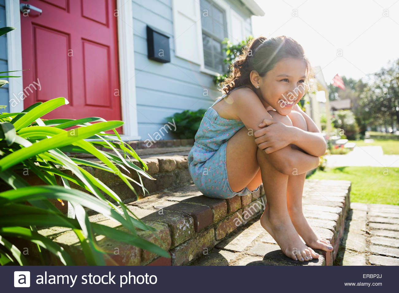 Smiling girl hugging knees on sunny front stoop Stock Photo - Alamy