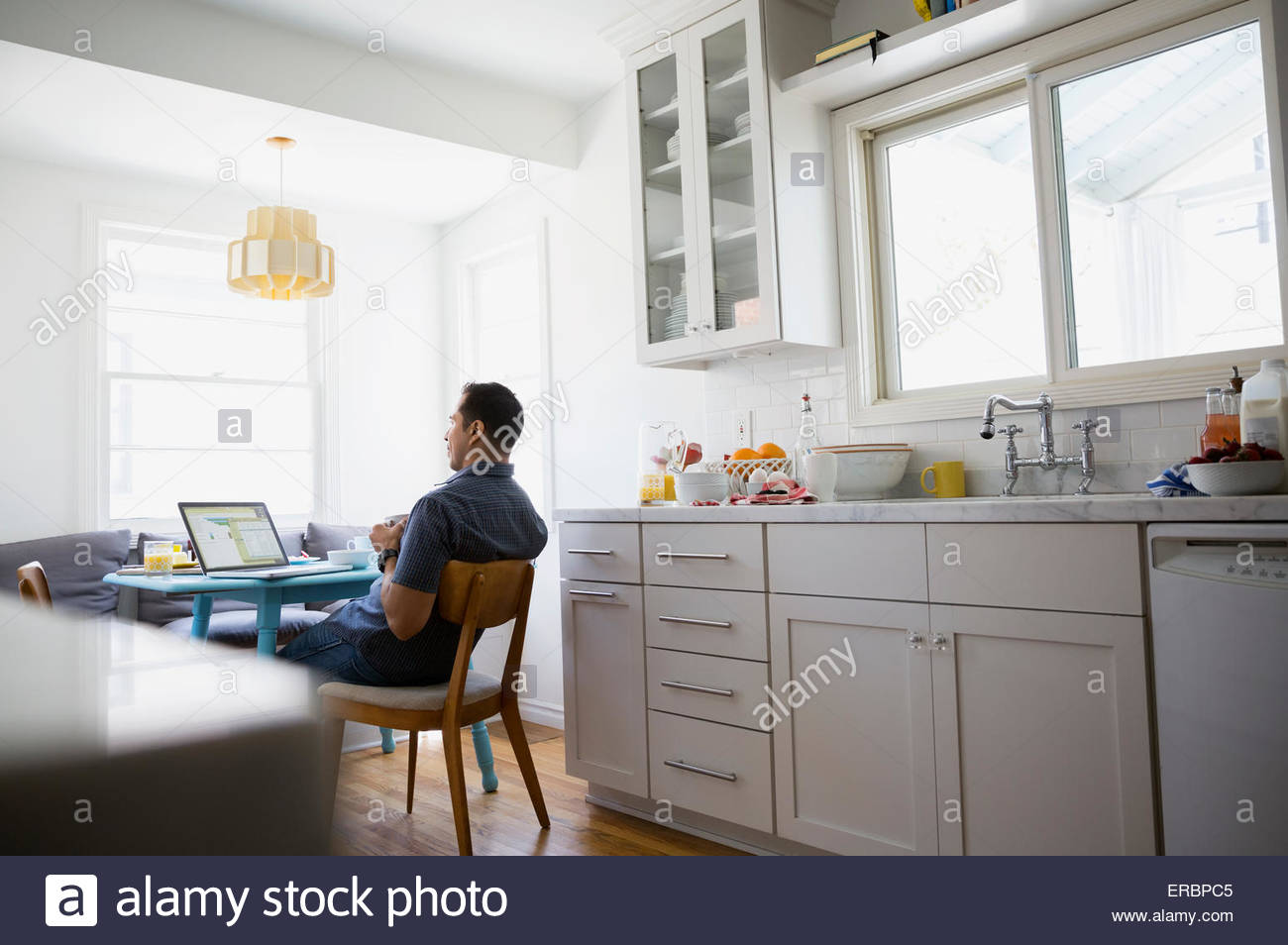 Brunette man working at laptop at kitchen table Stock Photo - Alamy