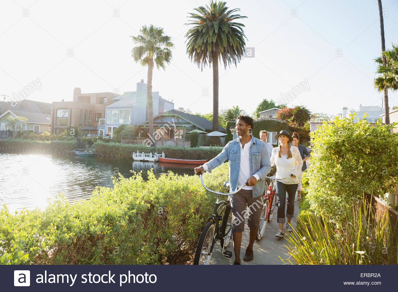 Friends walking bicycles on path along sunny canal Stock Photo - Alamy