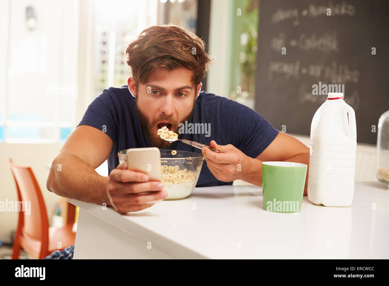 Young Man Eating Breakfast Whilst Using Mobile Phone Stock Photo - Alamy