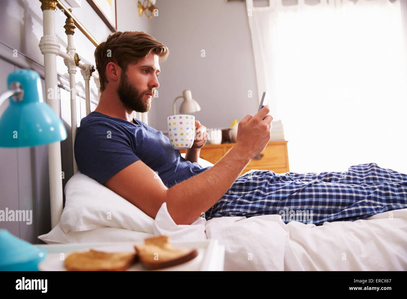 Man Eating Breakfast In Bed Whilst Using Mobile Phone Stock Photo - Alamy