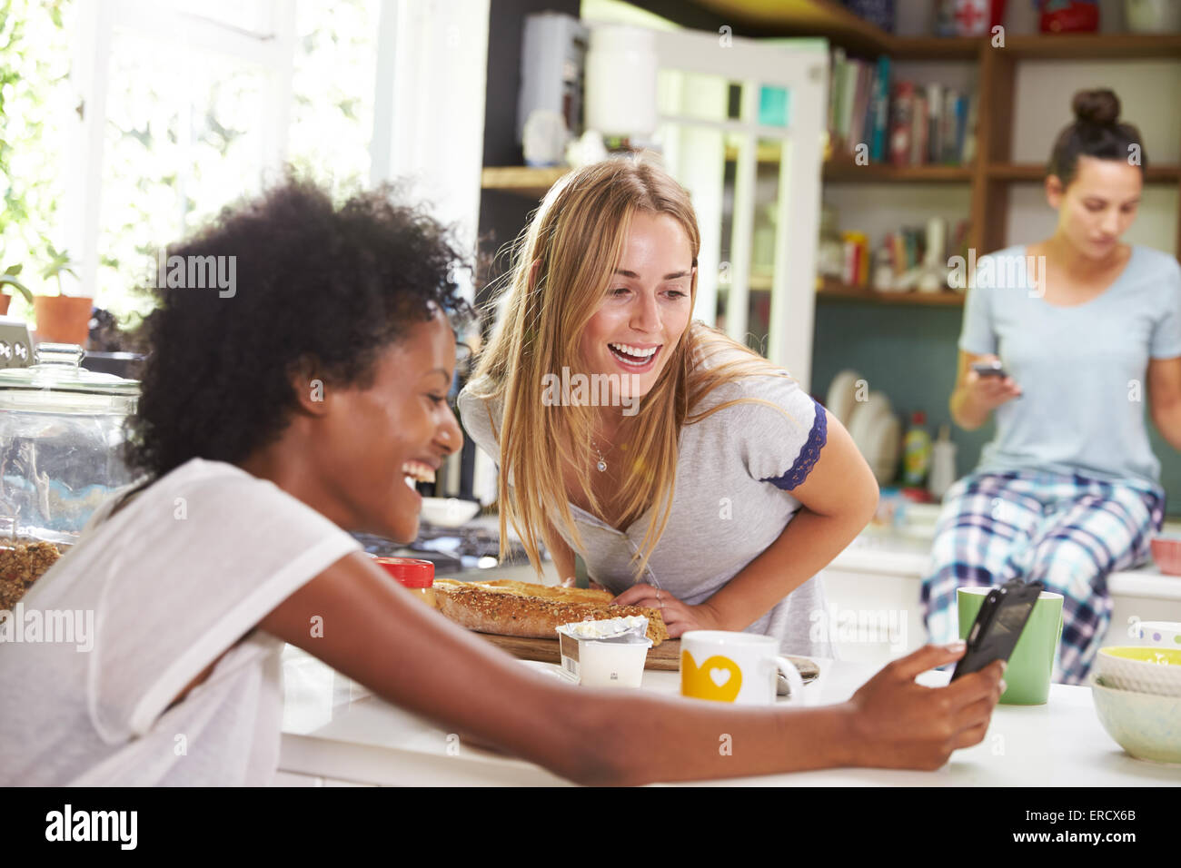 Female Friends Making Breakfast Whilst Checking Mobile Phone Stock ...