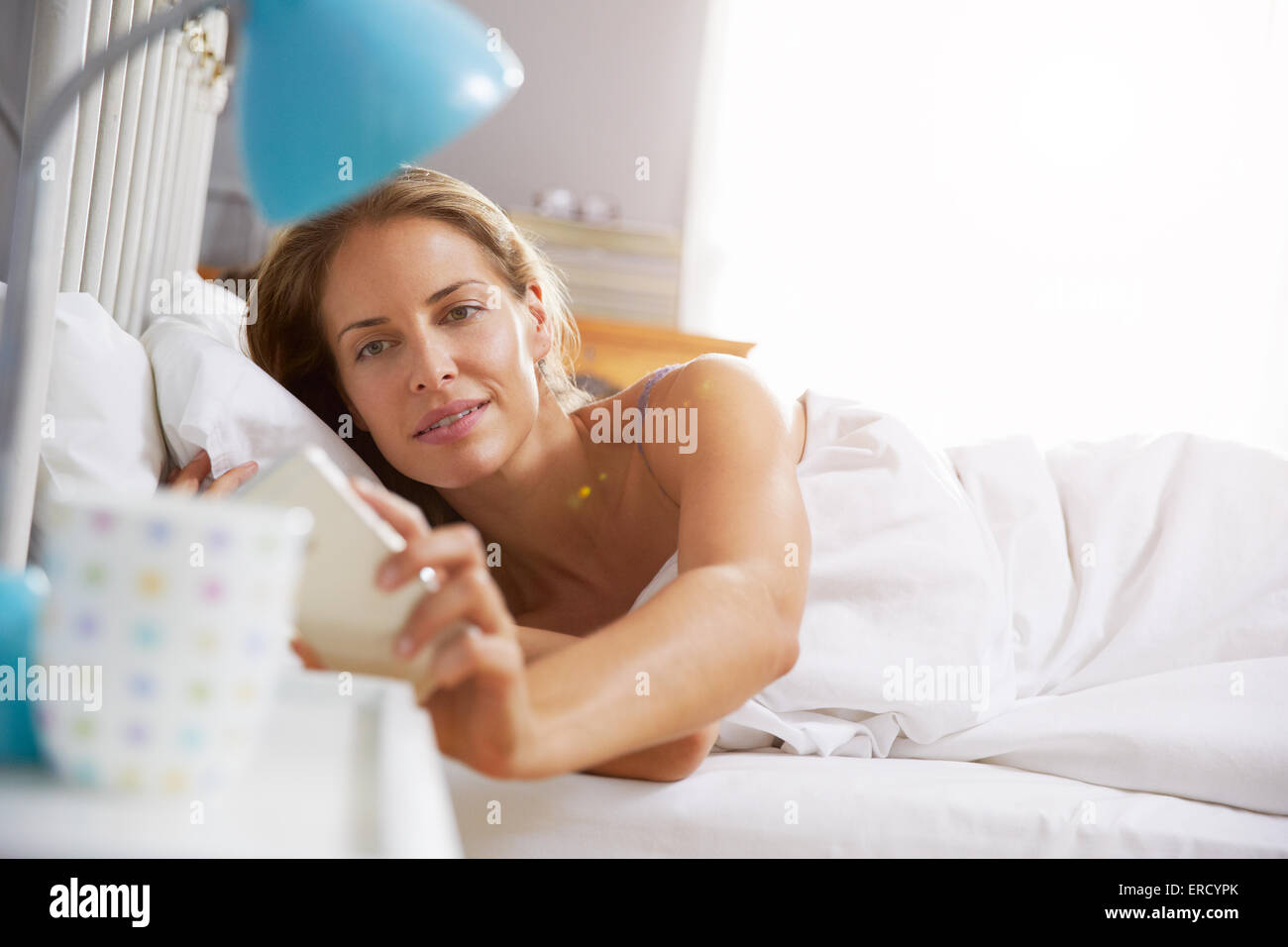 Woman Lying In Bed Reaching To Check Mobile Phone Stock Photo - Alamy
