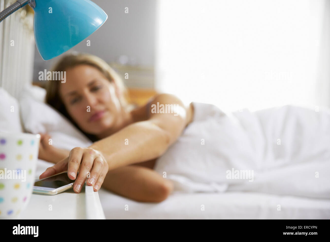 Woman Lying In Bed Reaching To Check Mobile Phone Stock Photo - Alamy