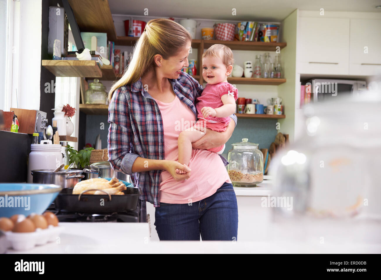 Mother Cooking Meal Whilst Holding Daughter In Kitchen Stock Photo - Alamy