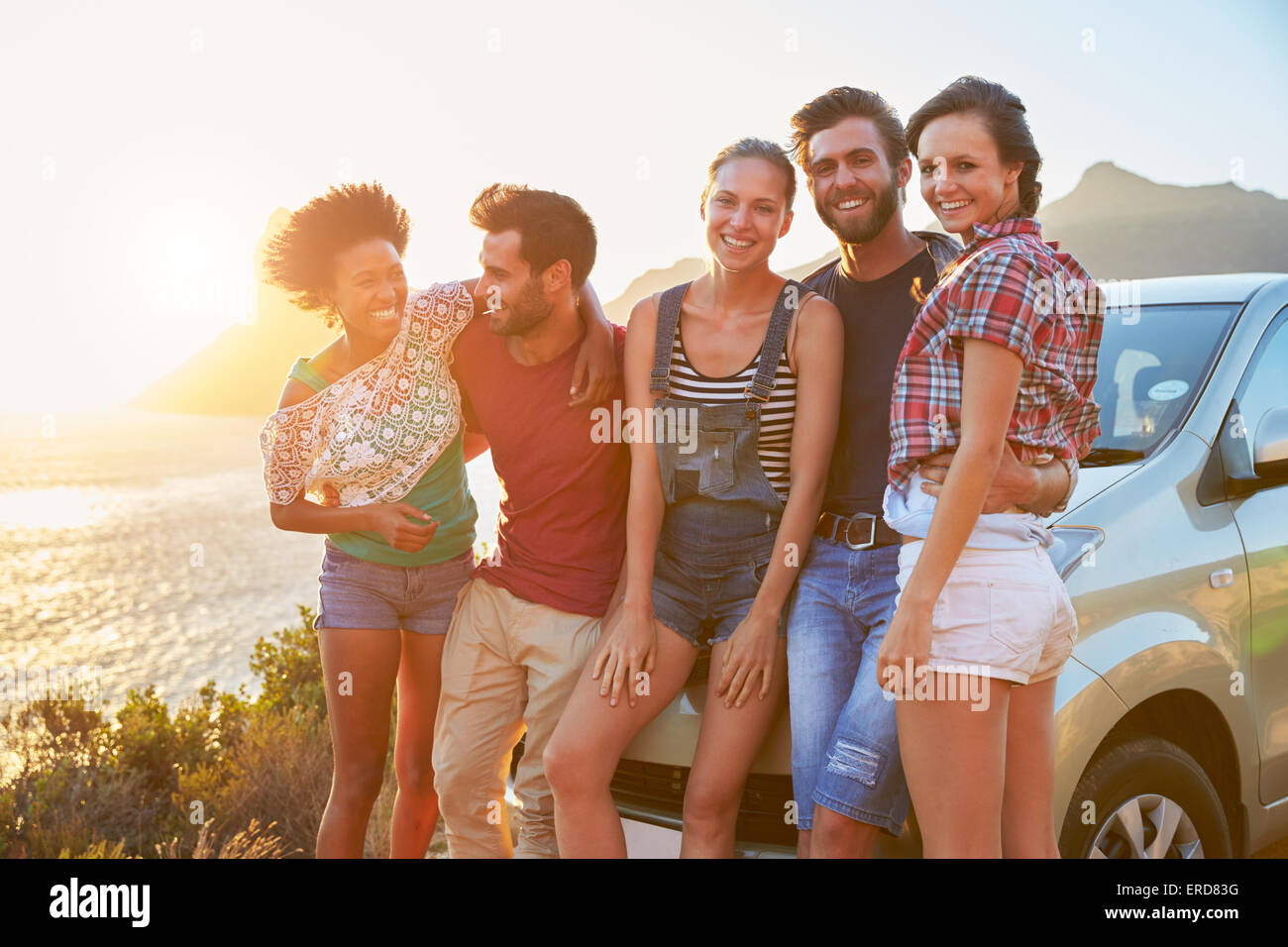 Group Of Friends Standing By Car On Coastal Road At Sunset Stock Photo ...