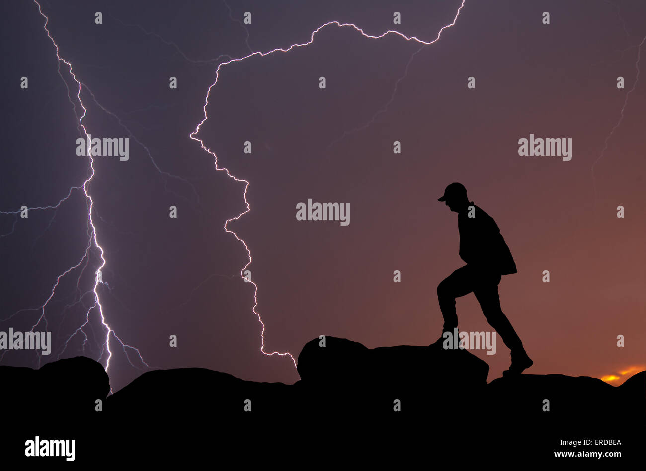 Silhouette of a man walking on top of a mountain, with lightning ...