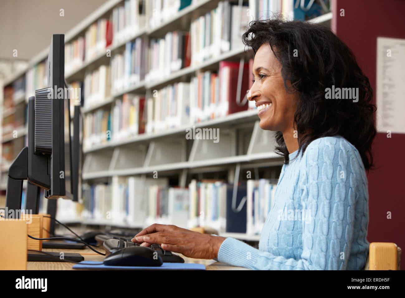 Mid age woman working on computer in library Stock Photo - Alamy