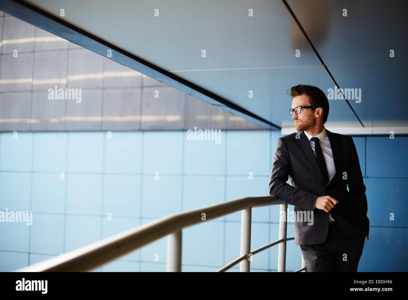 Businessman in suit standing by railings in office building Stock Photo ...