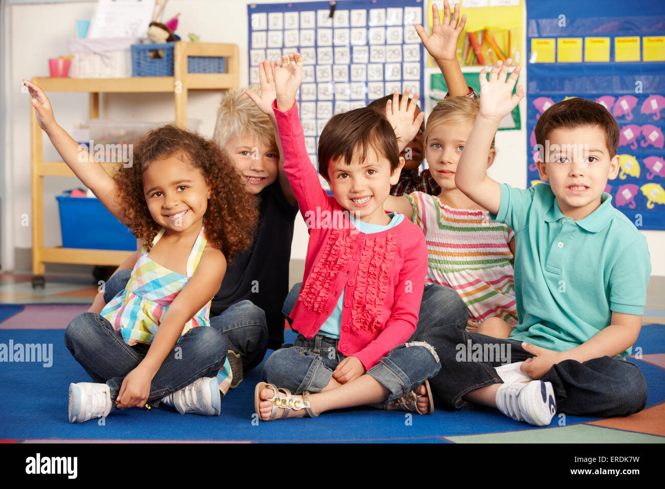 Group Of Elementary Age Schoolchildren Answering Question In Class ...