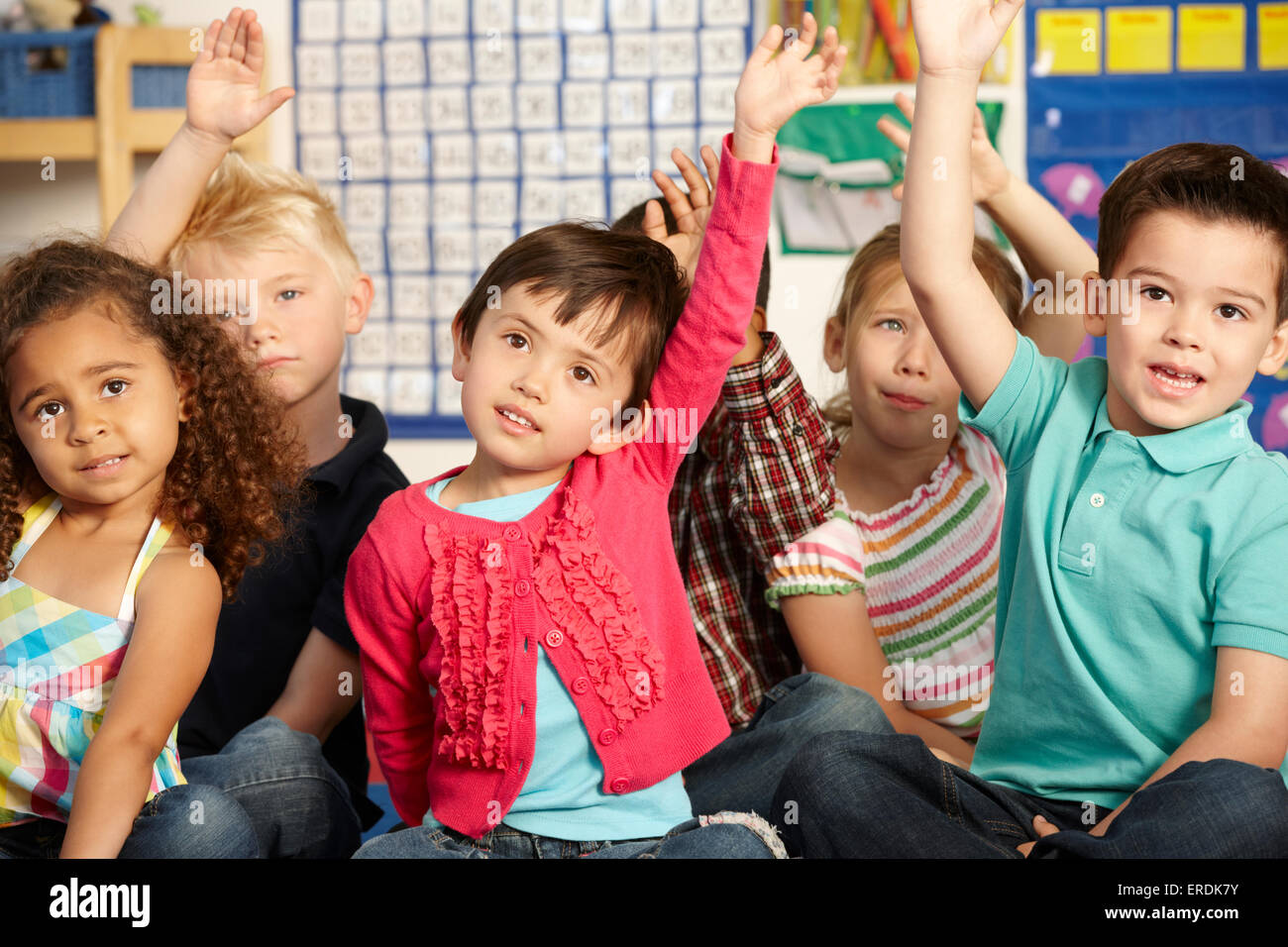 Group Of Elementary Age Schoolchildren Answering Question In Class ...