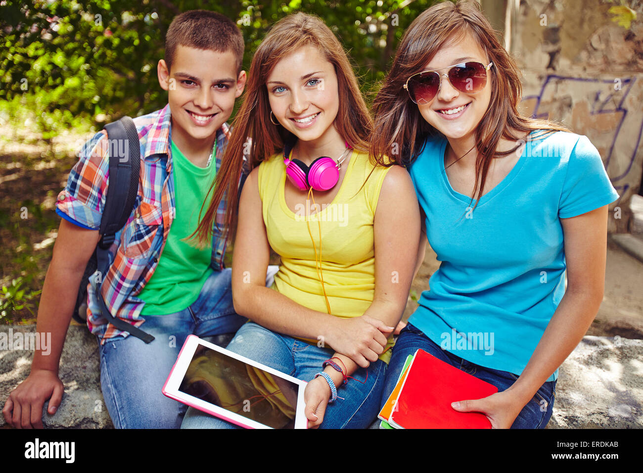 Smiling school friends sitting in park Stock Photo - Alamy