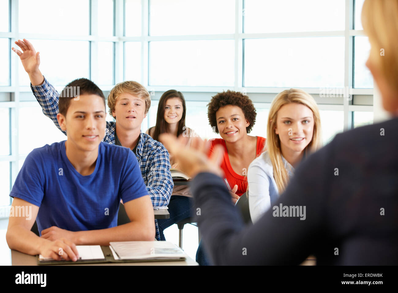Multi racial teenage pupils in class one with hand up Stock Photo - Alamy