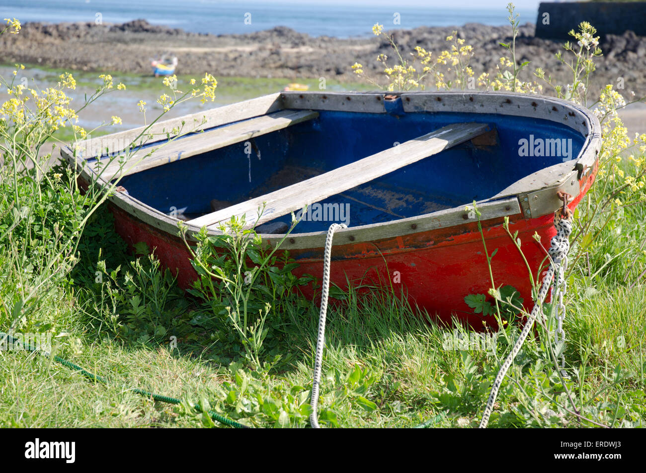 Blue and red wooden rowing boat abandoned on a beach in Guernsey Stock ...