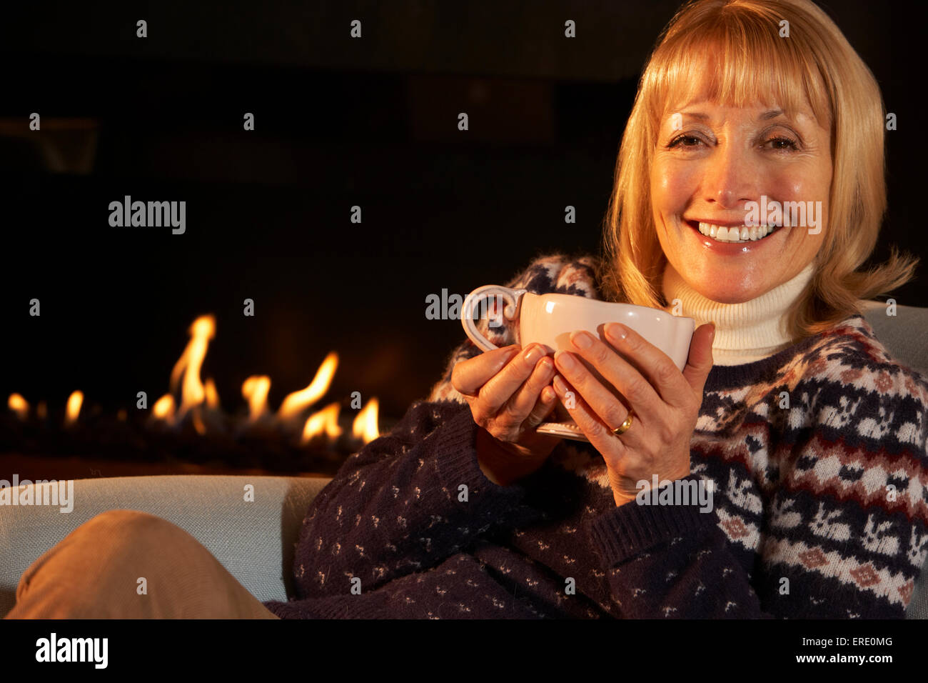 Mature woman relaxing in front of fire at home Stock Photo - Alamy