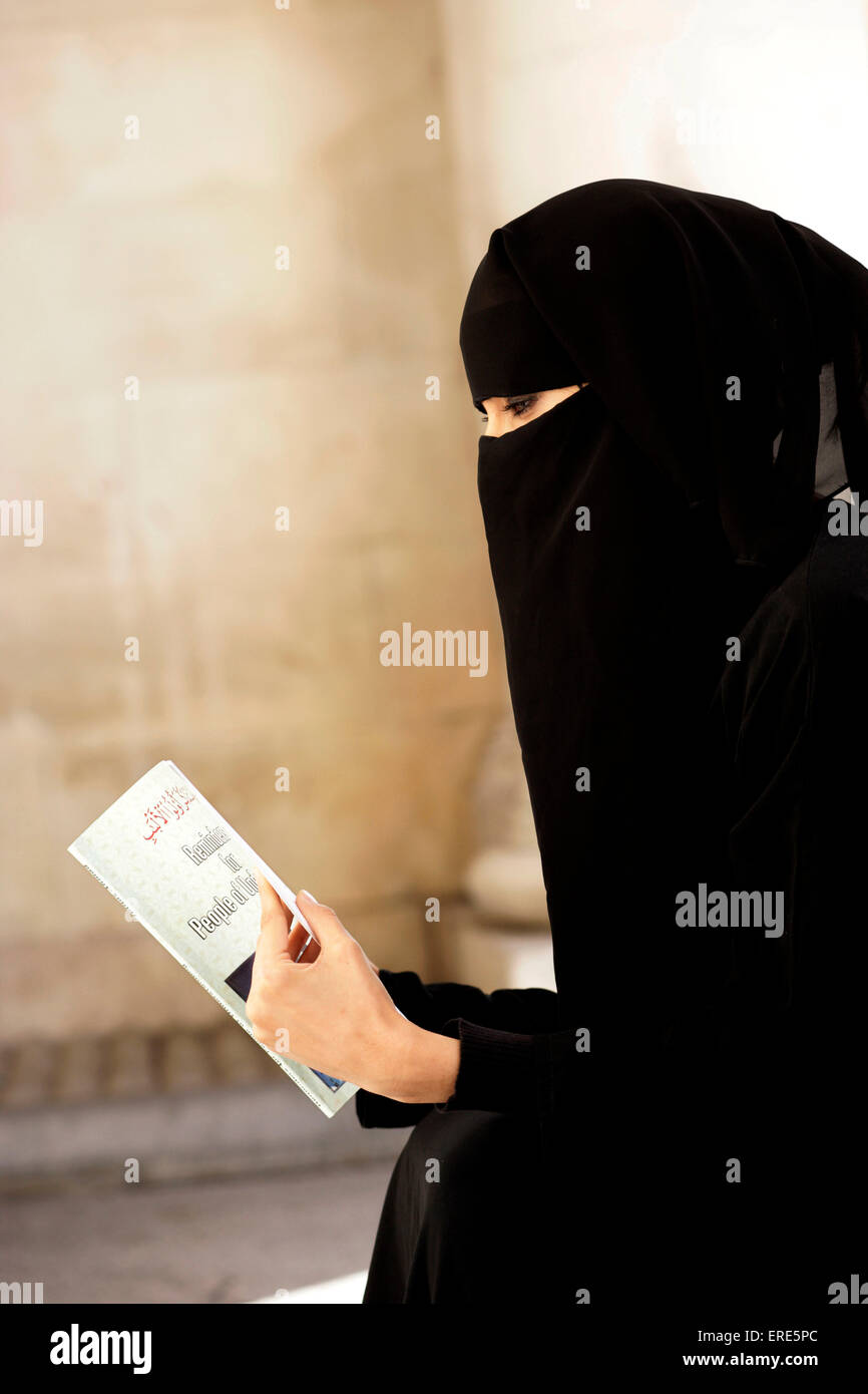 ALL USES TO STATE POSED BY MODEL Muslim woman wearing a burqa, reading ...