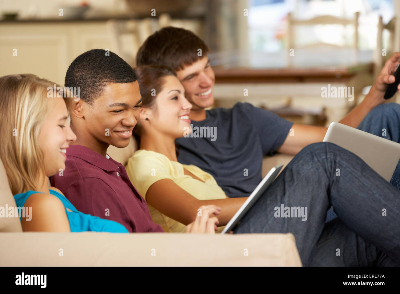 Four Teenagers Sitting On Sofa At Home Using Tablet Computer And Laptop ...