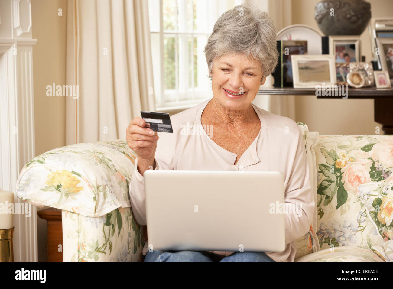 Retired Senior Woman Sitting On Sofa At Home Using Laptop To Make ...