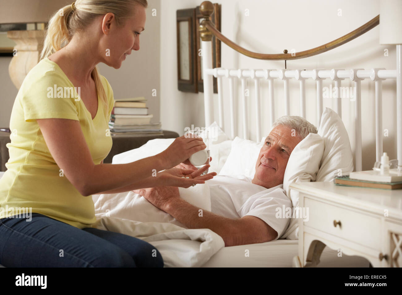 Adult Daughter Giving Senior Male Parent Medication In Bed At Home ...