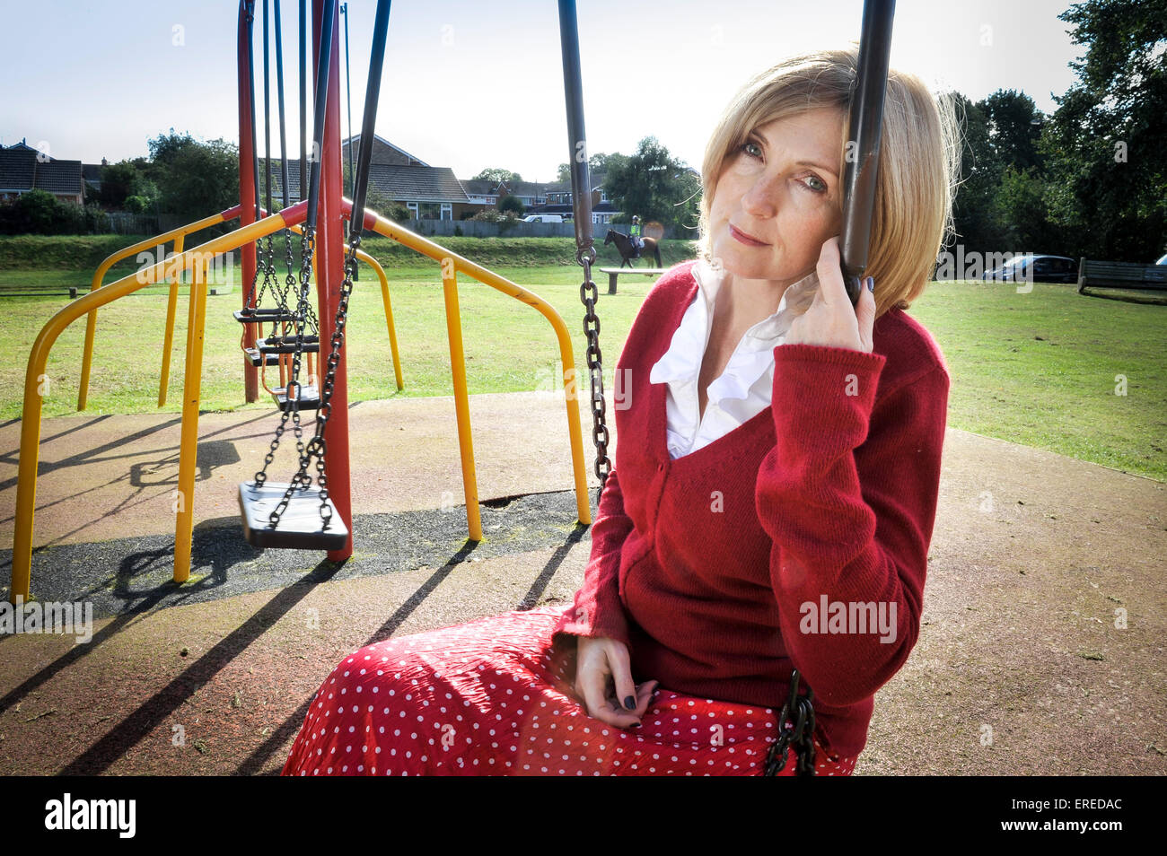 A woman in red sat on a swing in a park Stock Photo - Alamy