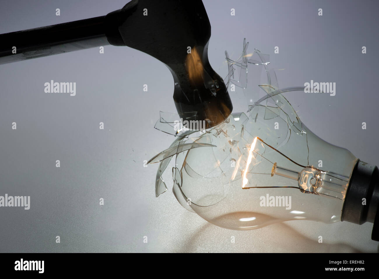 Light bulb being smashed by a hammer showing filament still glowing ...
