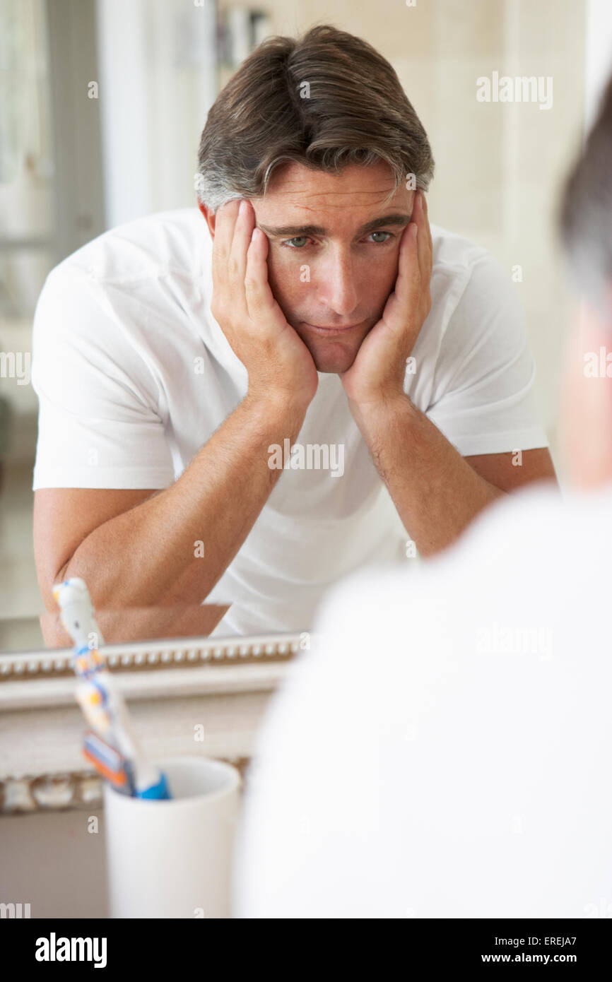Unhappy Man Looking At Reflection In Bathroom Mirror Stock Photo - Alamy