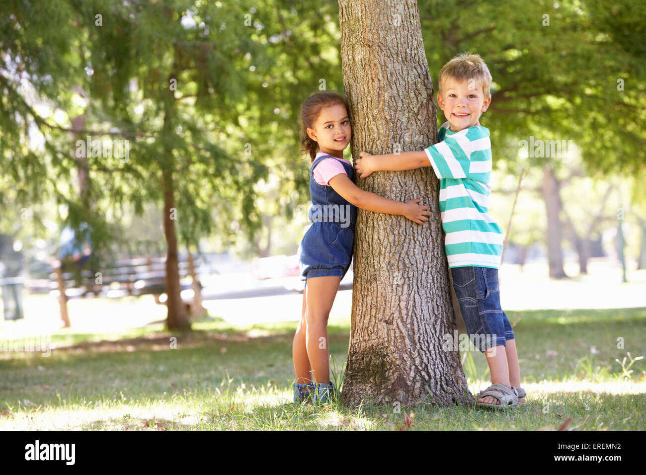 Two Children Hugging Tree In Park Stock Photo - Alamy