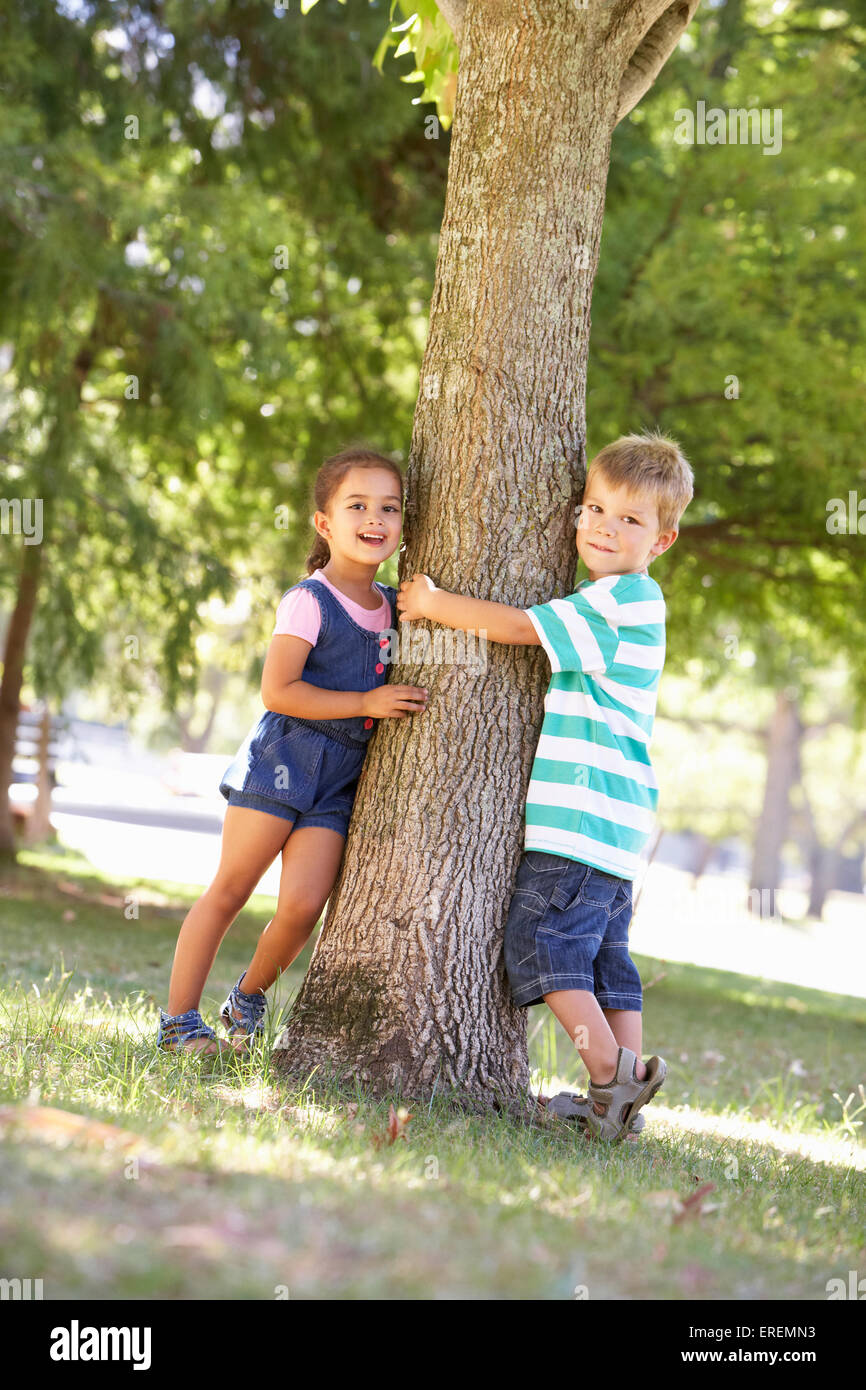 Two Children Hugging Tree In Park Stock Photo - Alamy
